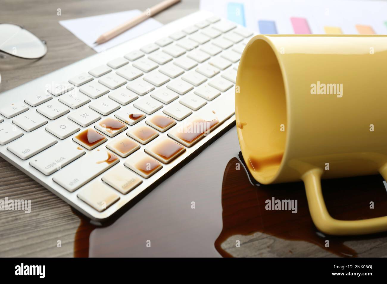 Cup of coffee spilled over computer keyboard on wooden office desk ...