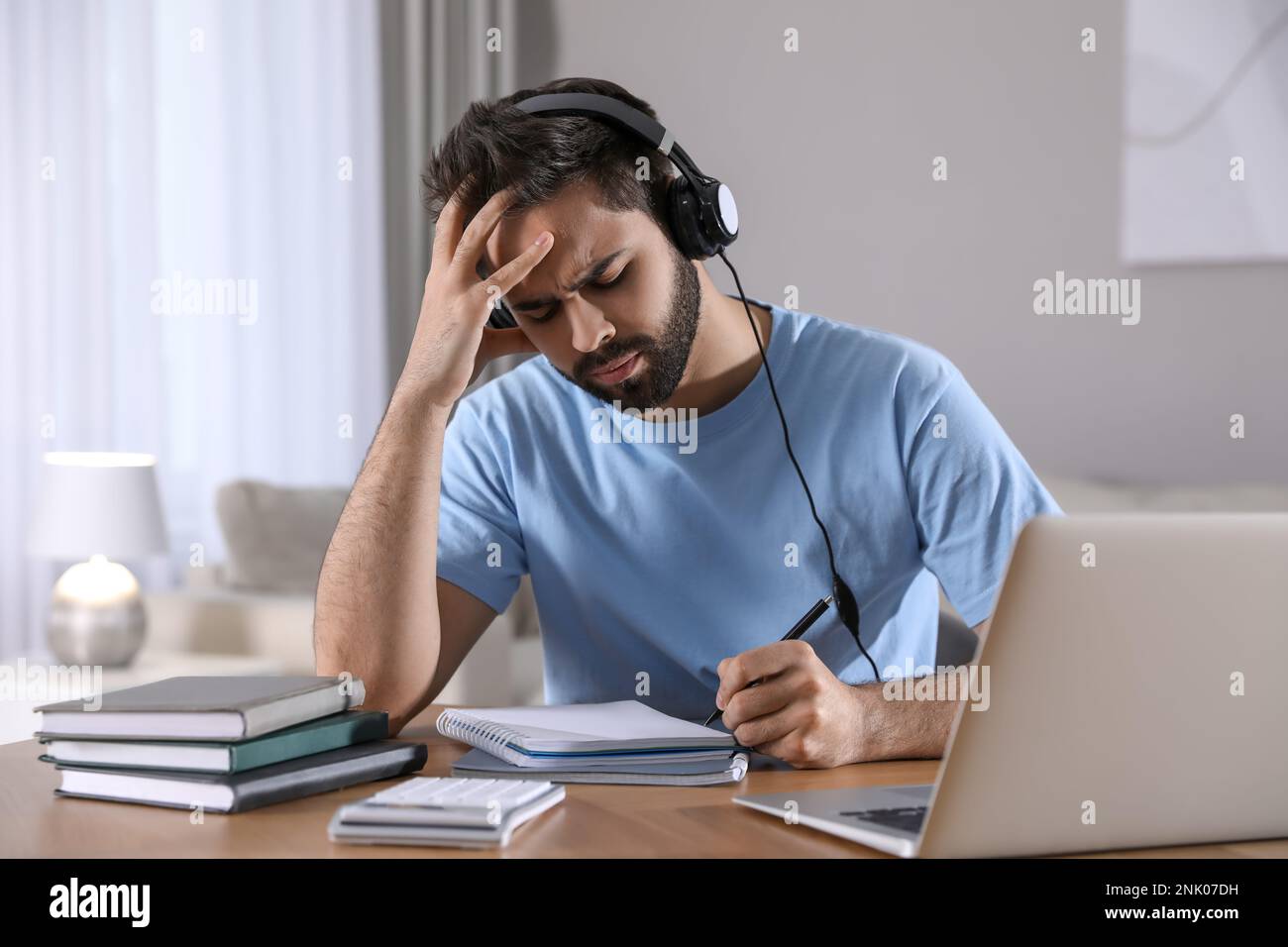 Confused young man writing down notes during webinar at table in room ...