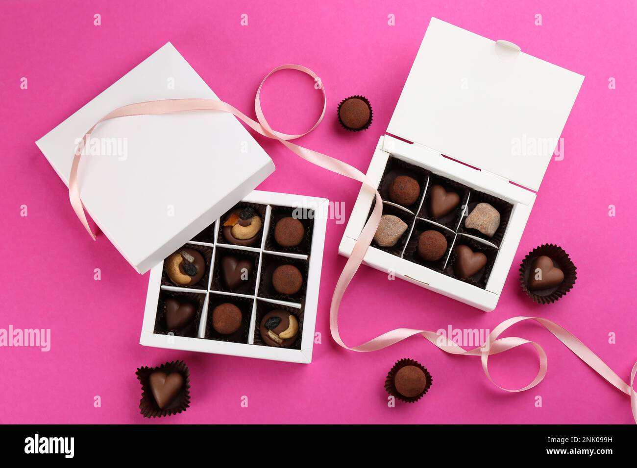 Different delicious chocolate candies in boxes on pink background, flat ...
