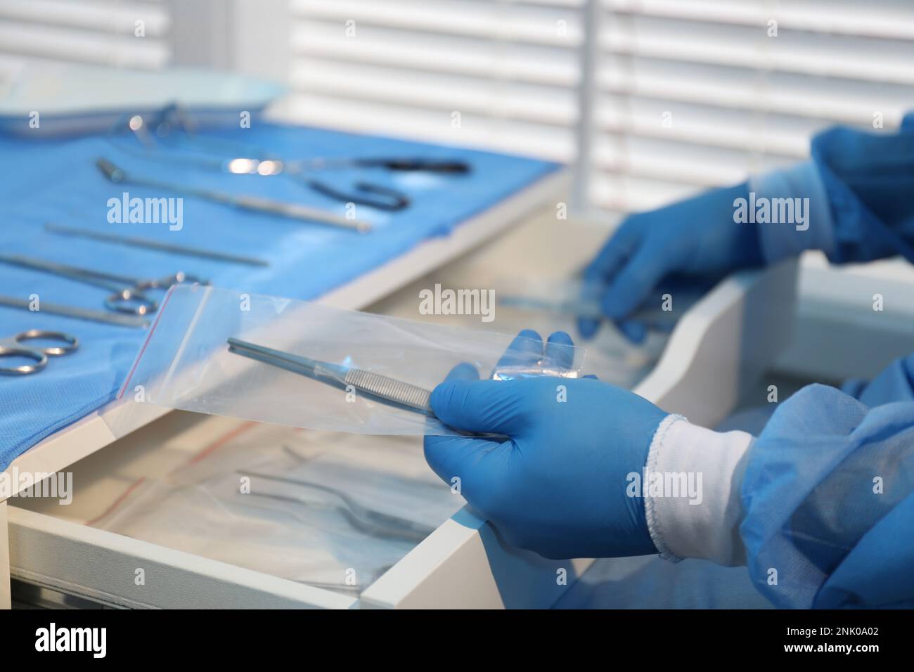 Doctor putting medical forceps into drawer indoors, closeup. Table with ...