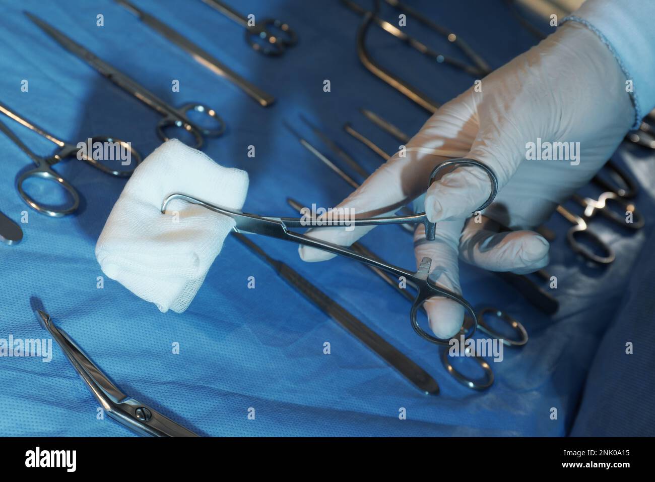 Doctor holding medical clamps with pad near table of different surgical ...