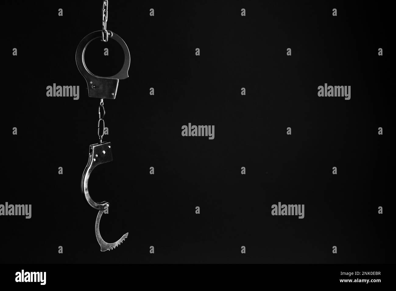 Classic chain handcuffs hanging on black background, space for text ...