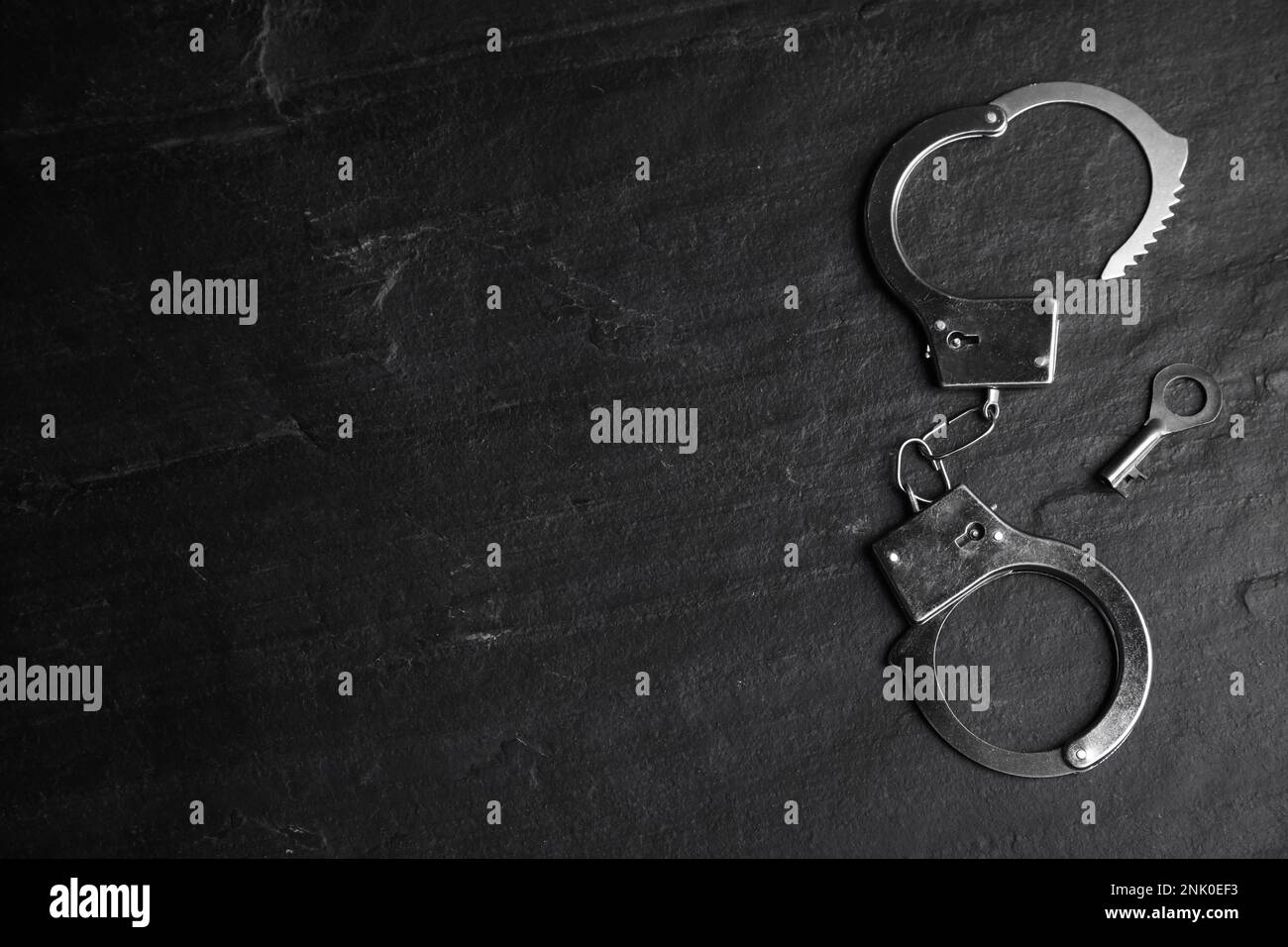 Classic chain handcuffs with key on black table, flat lay. Space for ...