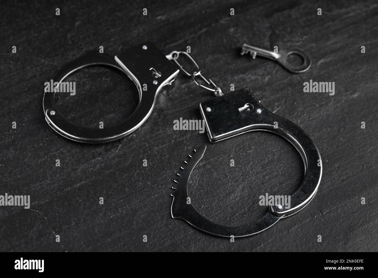 Classic chain handcuffs with key on black table Stock Photo - Alamy