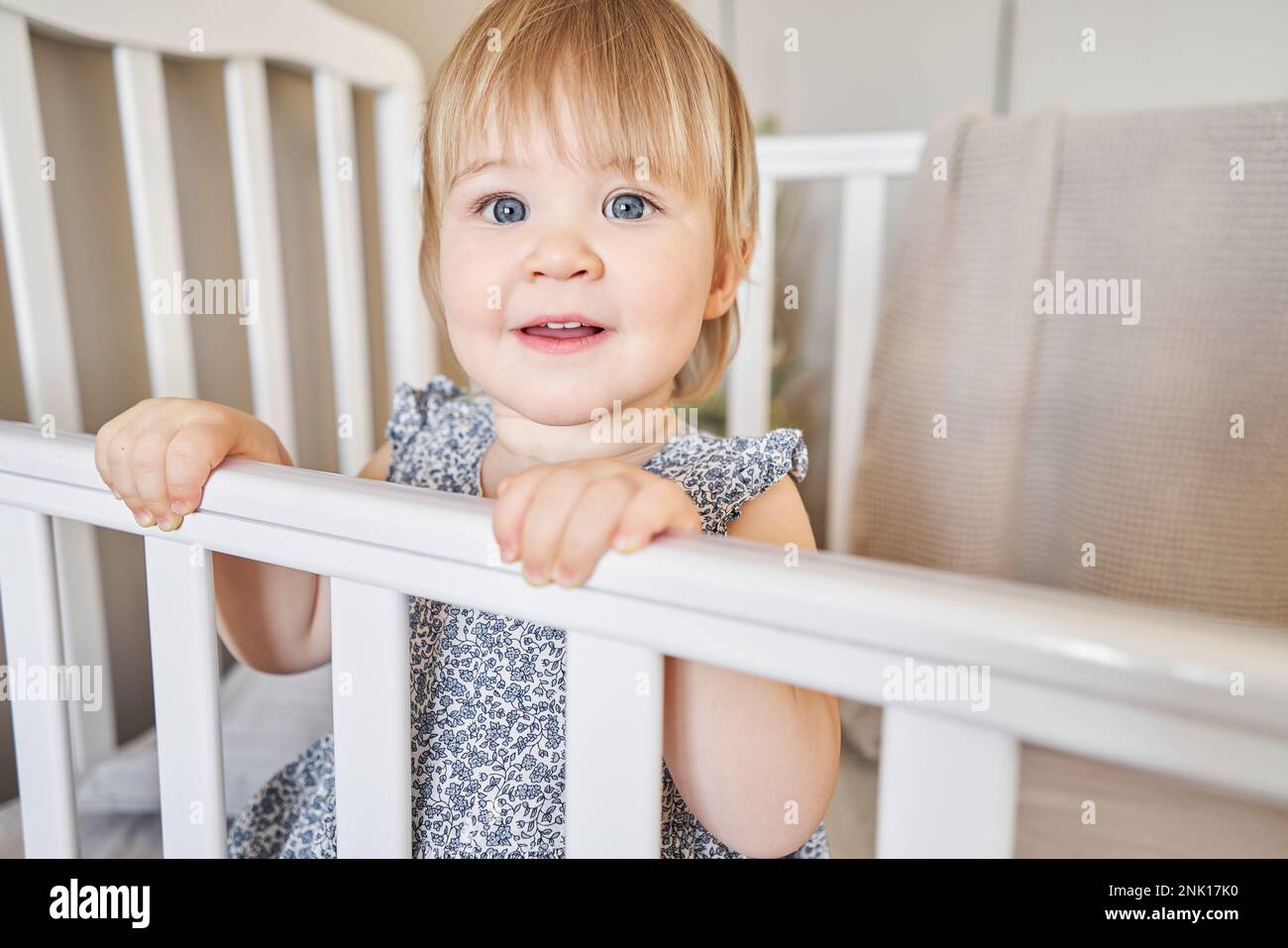 Happy baby girl one and half standing in the crib. Smiling 18 months ...