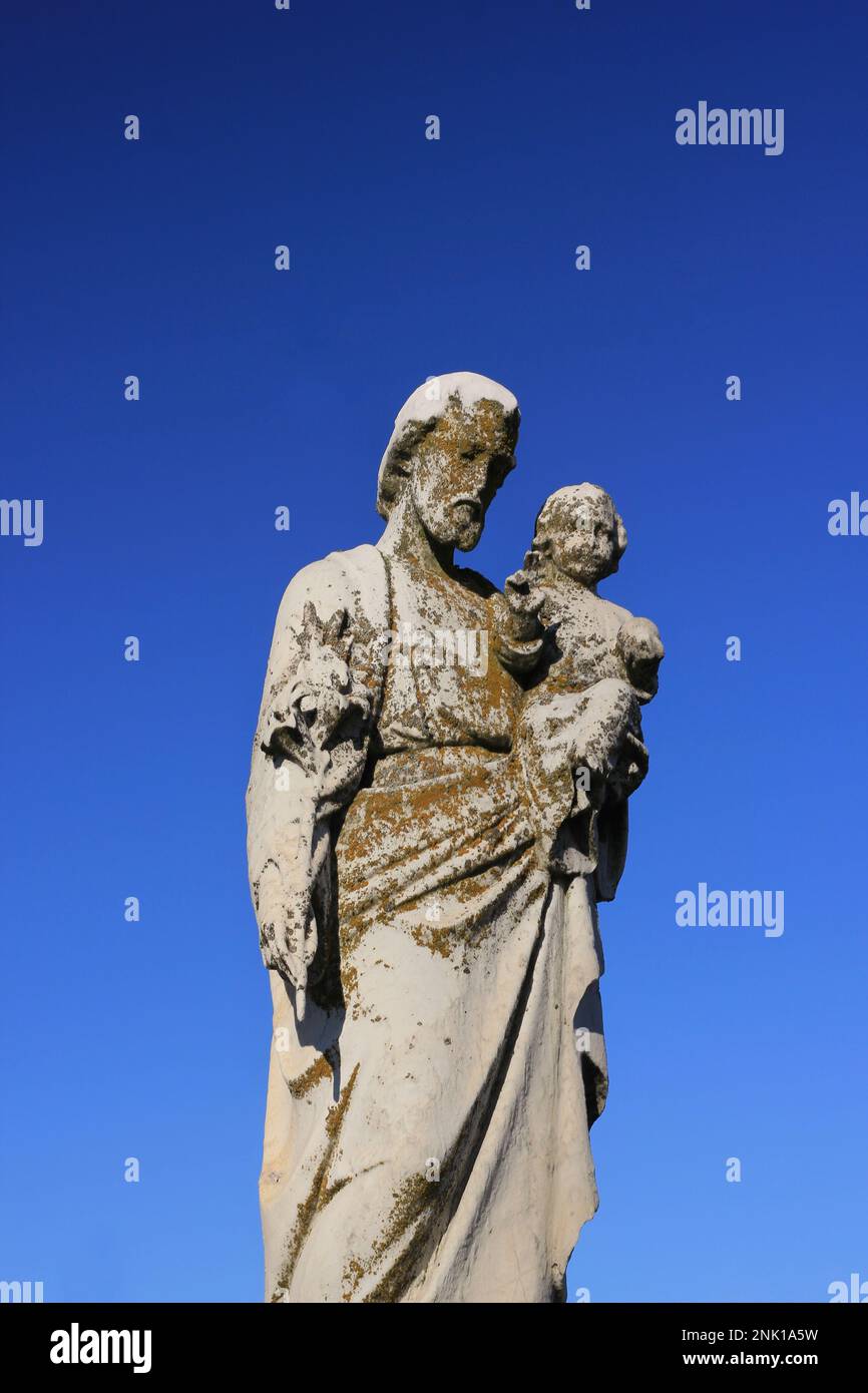 A worn and weathered natural stone statue of Saint Joseph carrying the ...