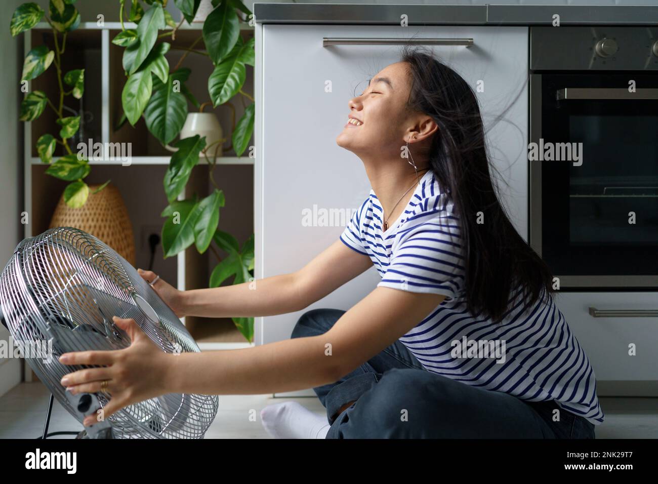 Happy joyful Asian girl sitting in front of electric fan, refreshing ...