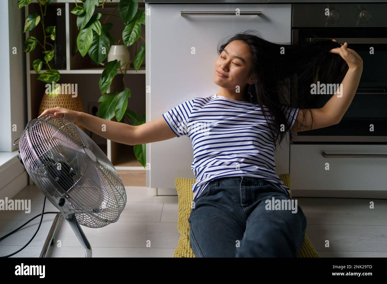 Young happy satisfied Asian girl relaxing under electric floor fan at ...