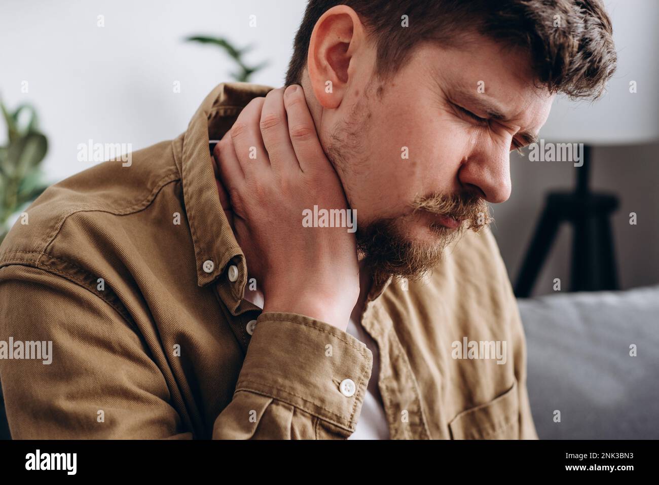 Close up of unhappy caucasian male holding hand on neck, suffering from ...