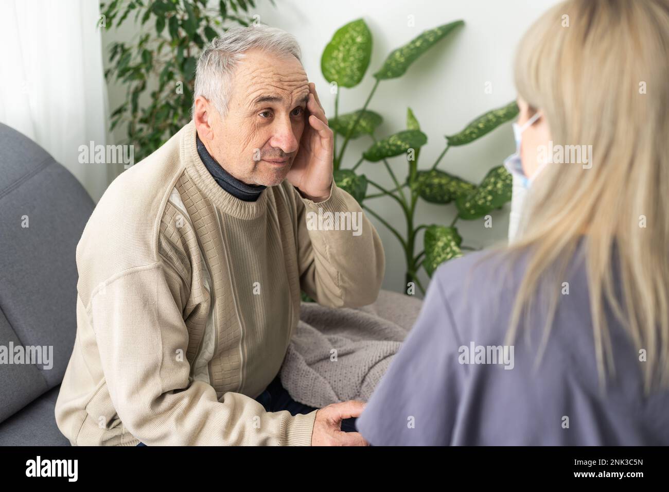 Caring nurse talks to old patient holds his hand sit in living room at ...