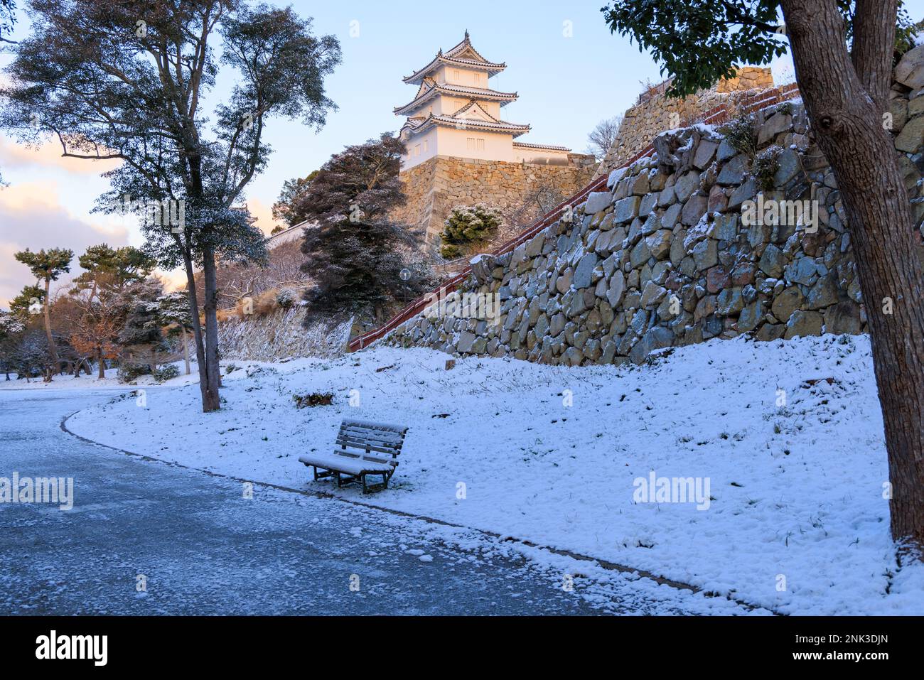 Historic Japanese castle towers over snow covered bench along path in ...