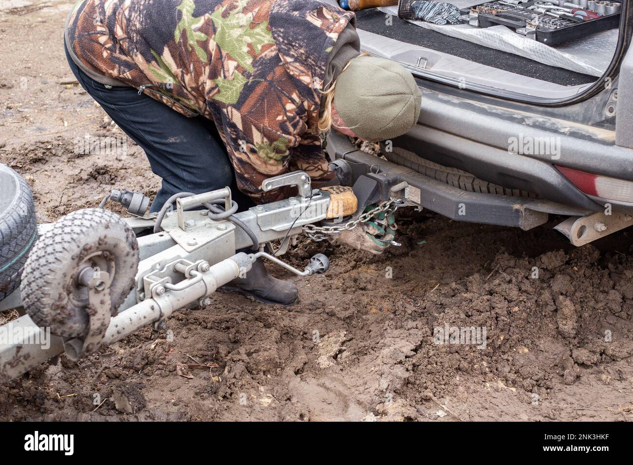 A man checking the hitch mechanism on a car trailer in bad weather ...