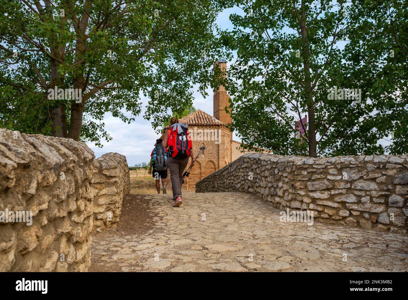 Pilgrims walk across a stone bridge leading to the Ermita de la Virgen ...