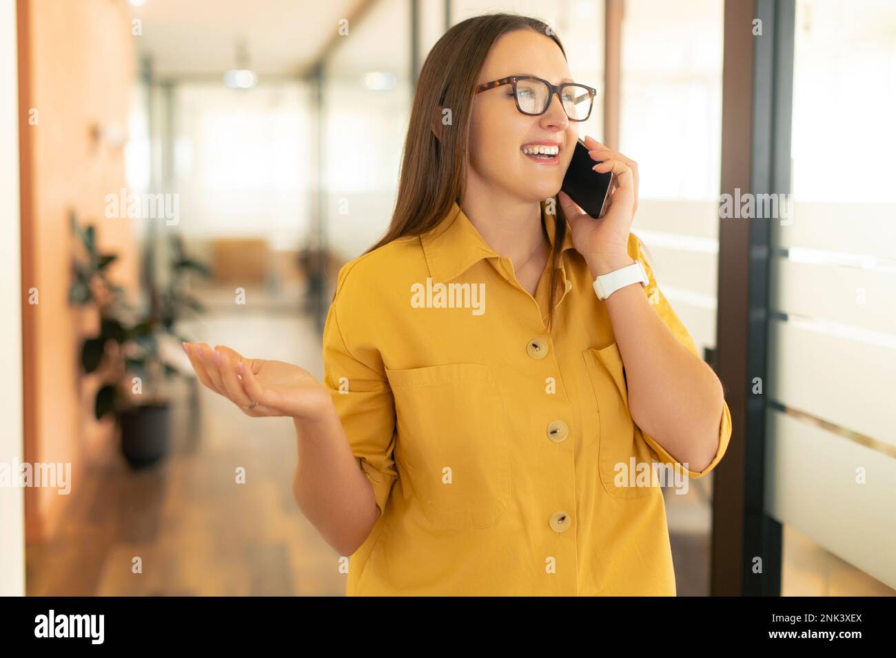 Happy cheerful female office employee talking on mobile phone and smiling, expressing positive ...