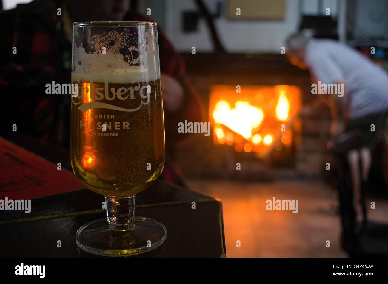 A pint of Carlsberg lager at the bar in the pub with a burning log fire ...