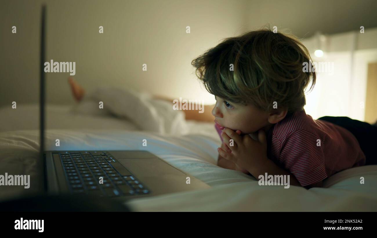 Child watching entertainment media on laptop screen laying in bed at ...