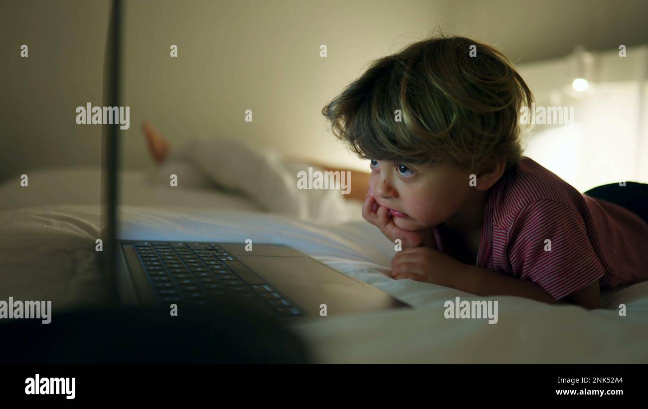 Child watching entertainment media on laptop screen laying in bed at ...