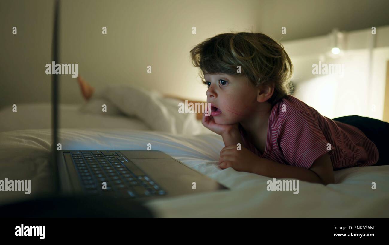 Child watching entertainment media on laptop screen laying in bed at ...