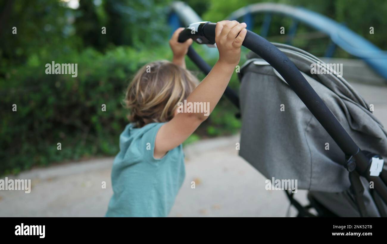 Cute little boy pushing stroller chair outside. Child pushes carriage ...