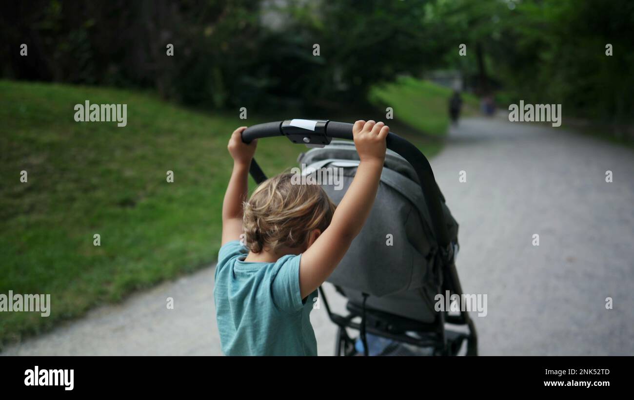 Cute little boy pushing stroller chair outside. Child pushes carriage ...