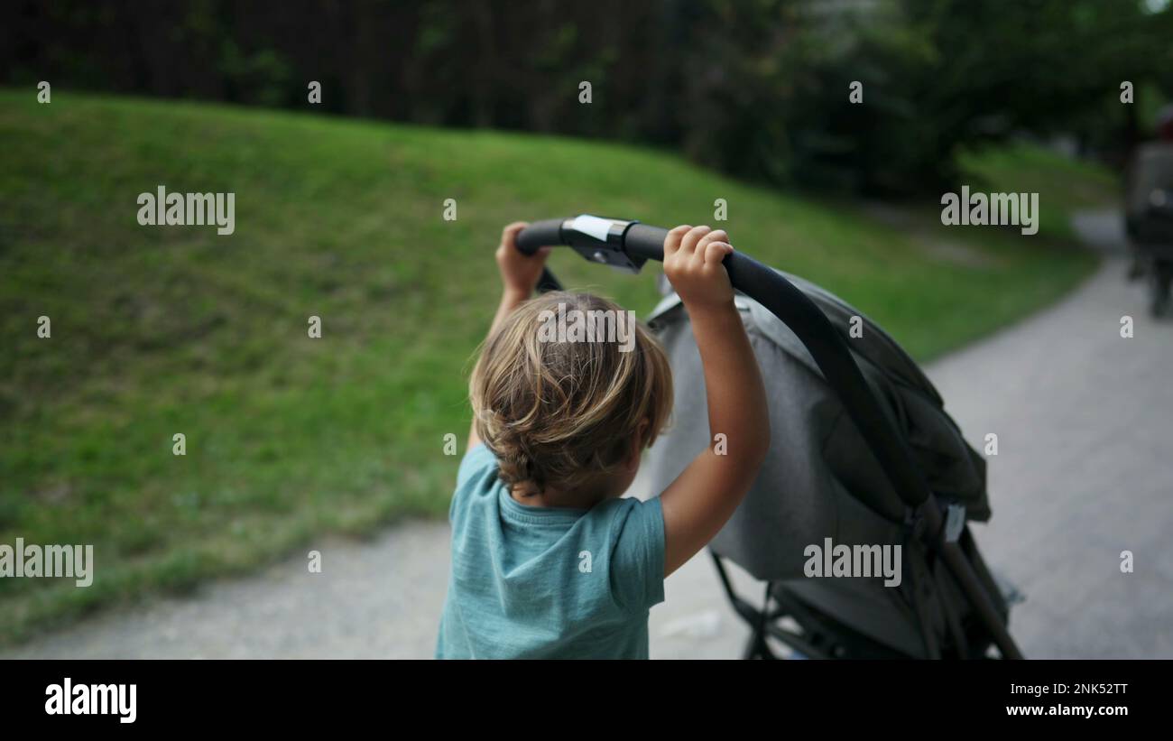 Cute little boy pushing stroller chair outside. Child pushes carriage ...