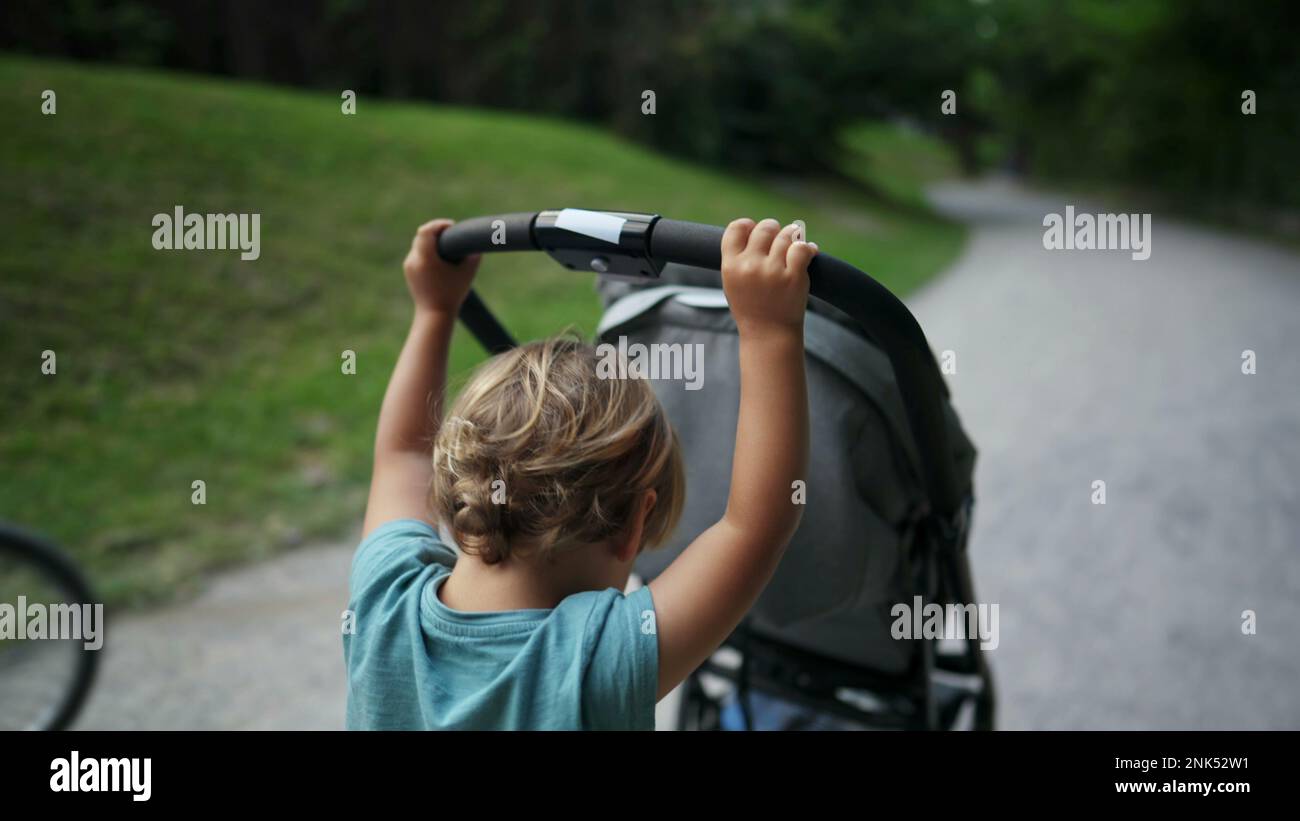 Cute little boy pushing stroller chair outside. Child pushes carriage ...