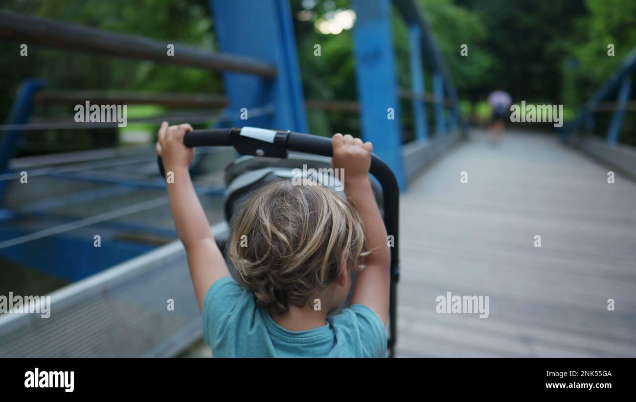 Adorable small boy helping to push stroller outside at park. Family ...