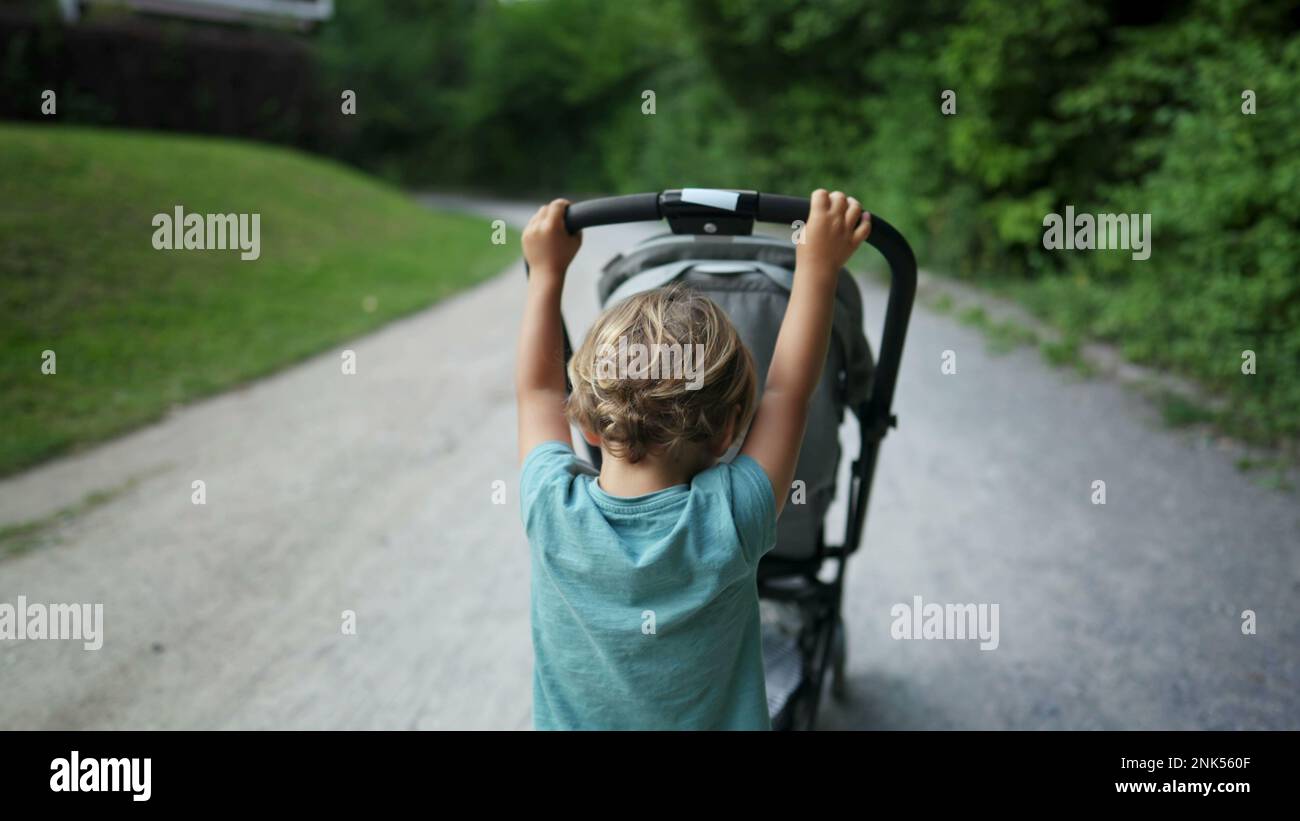 Back of kid pushing baby carriage outdoors in nature. Family outdoors ...