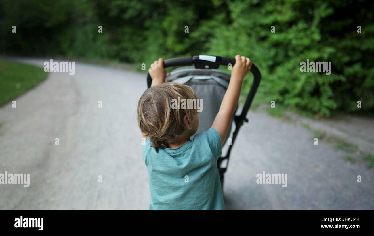 Back of kid pushing baby carriage outdoors in nature. Family outdoors ...