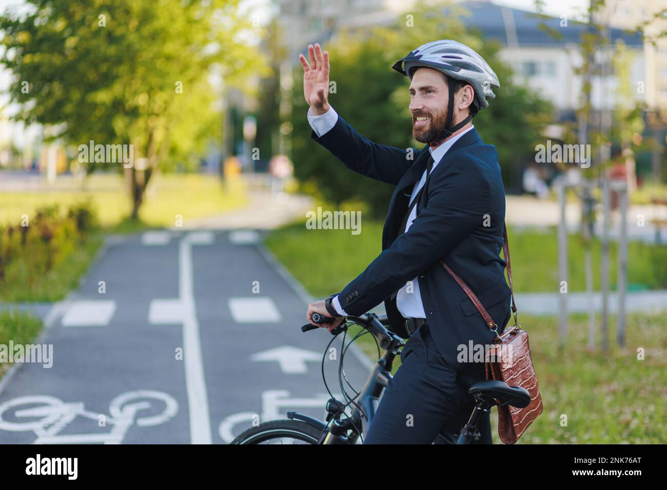 Joyful entrepreneur standing on cycle path with bike, waving goodbye to ...