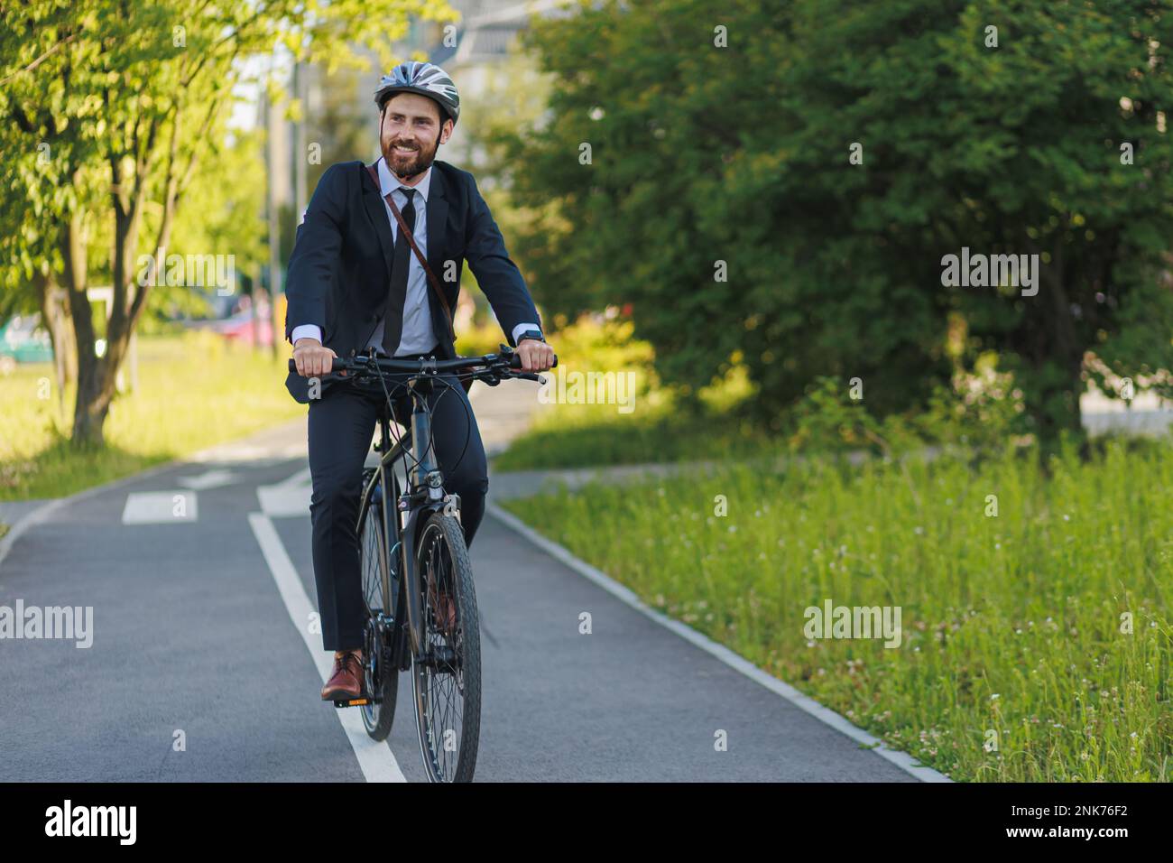 Handsome young executive in elegant suit riding on bike lane in sunny ...