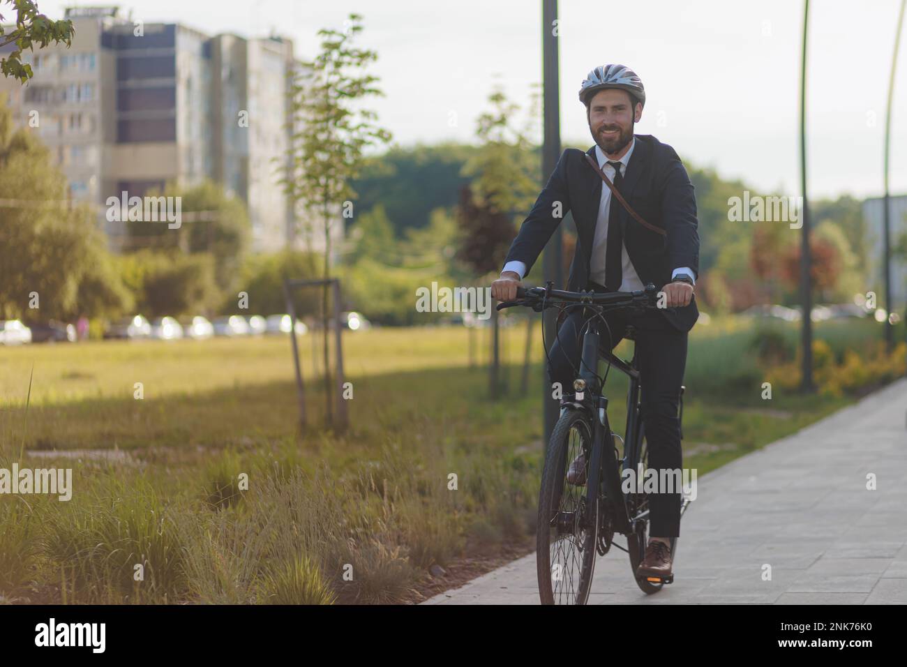 Joyful man in black suit riding on bike on paved road after workday in ...