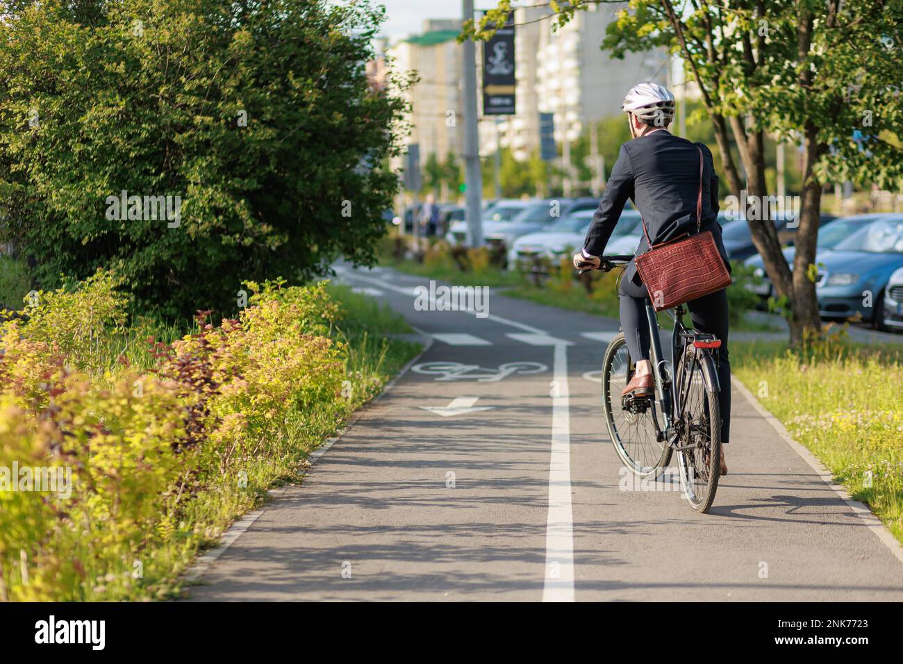 Stylish business man in helmet and suit cycling on bike path in sunny ...