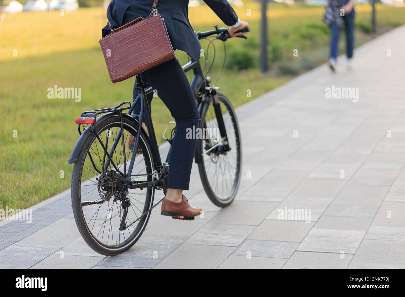 Back view of stylish man in suit cycling on bike on paved road outdoors ...