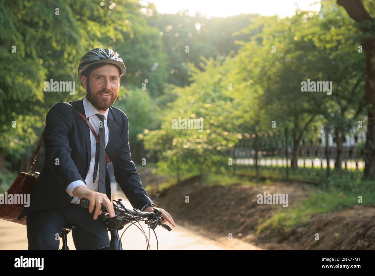 Smiling brunet male office worker riding on bike to work in warm sunny ...