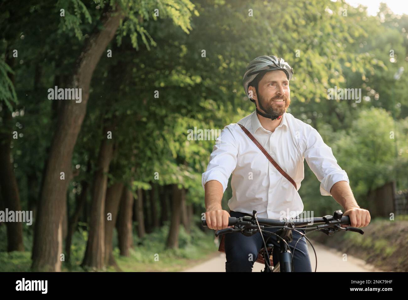 Happy male employee wearing helmet, riding on bike along alley, while ...