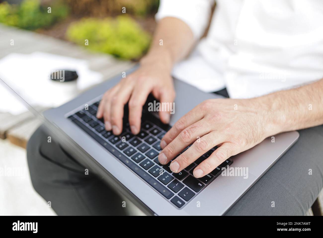 Cropped view of man sitting outdoors while using modern laptop for ...