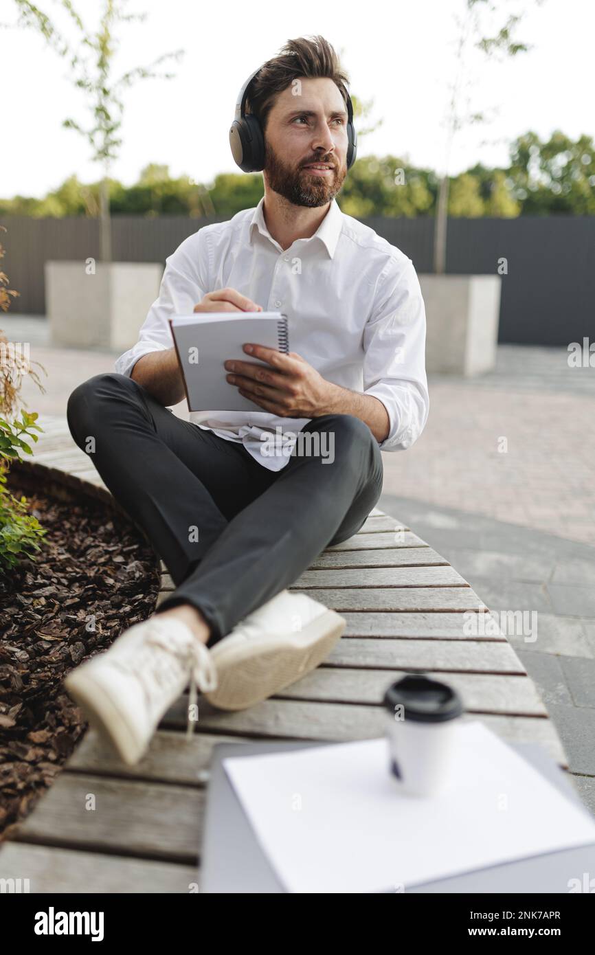 Stylish businessman in wireless headphones writing down own ideas in ...