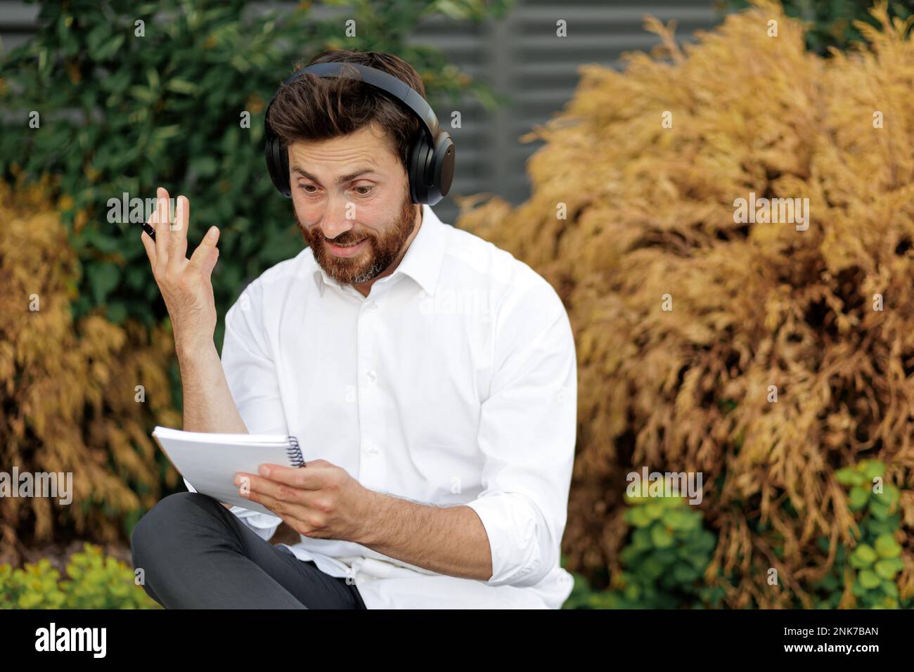 Surprised man in headphones raising hand, while checking notepad in ...
