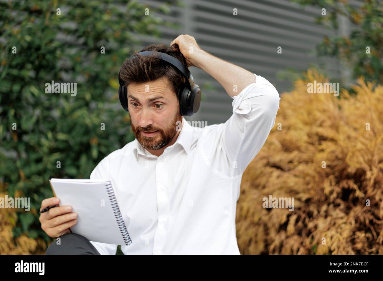 Puzzled entrepreneur in headphones scratching head, having difficulties ...