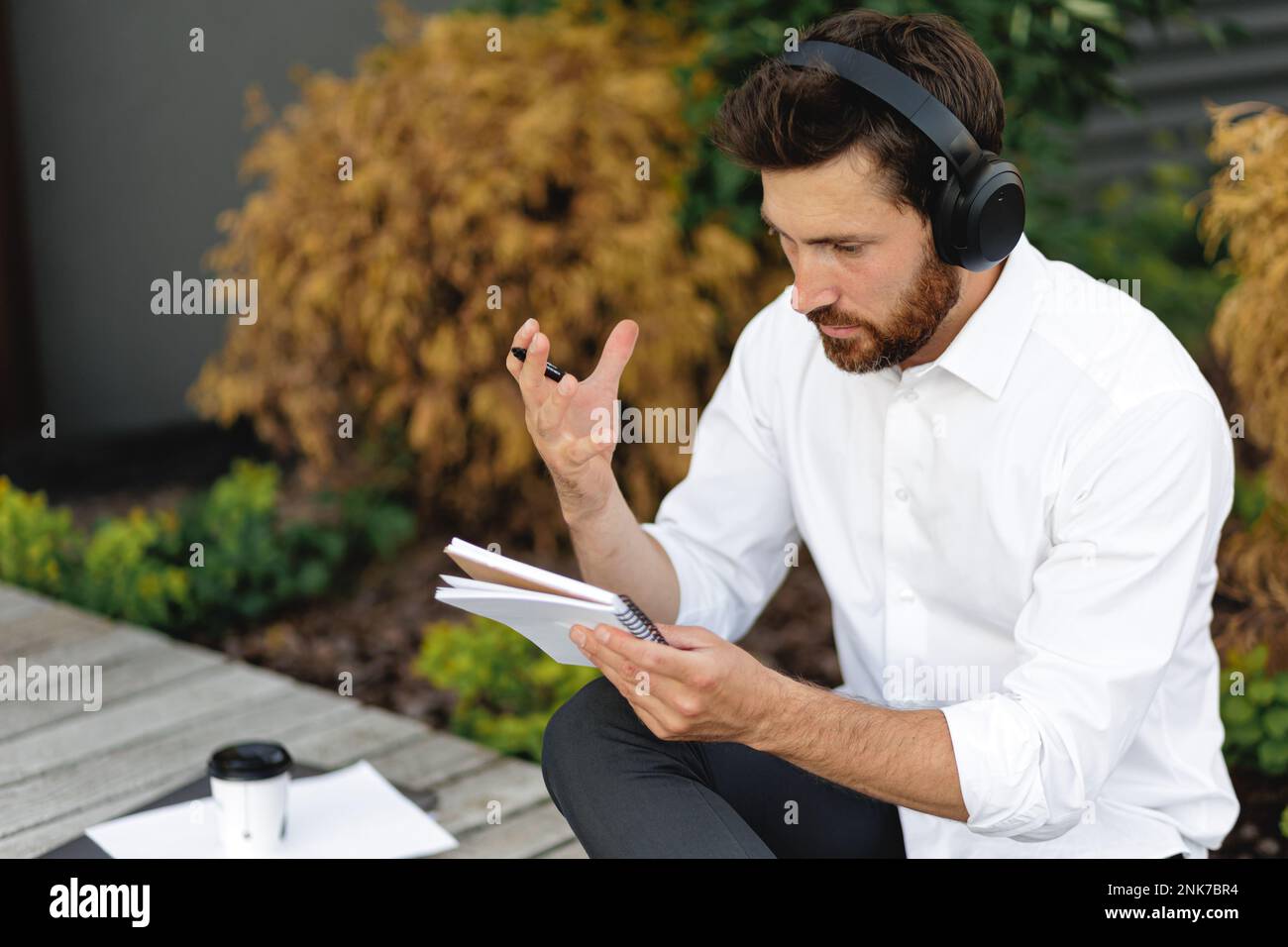 Thoughtful man in headphones checking notes, while sitting on bench ...
