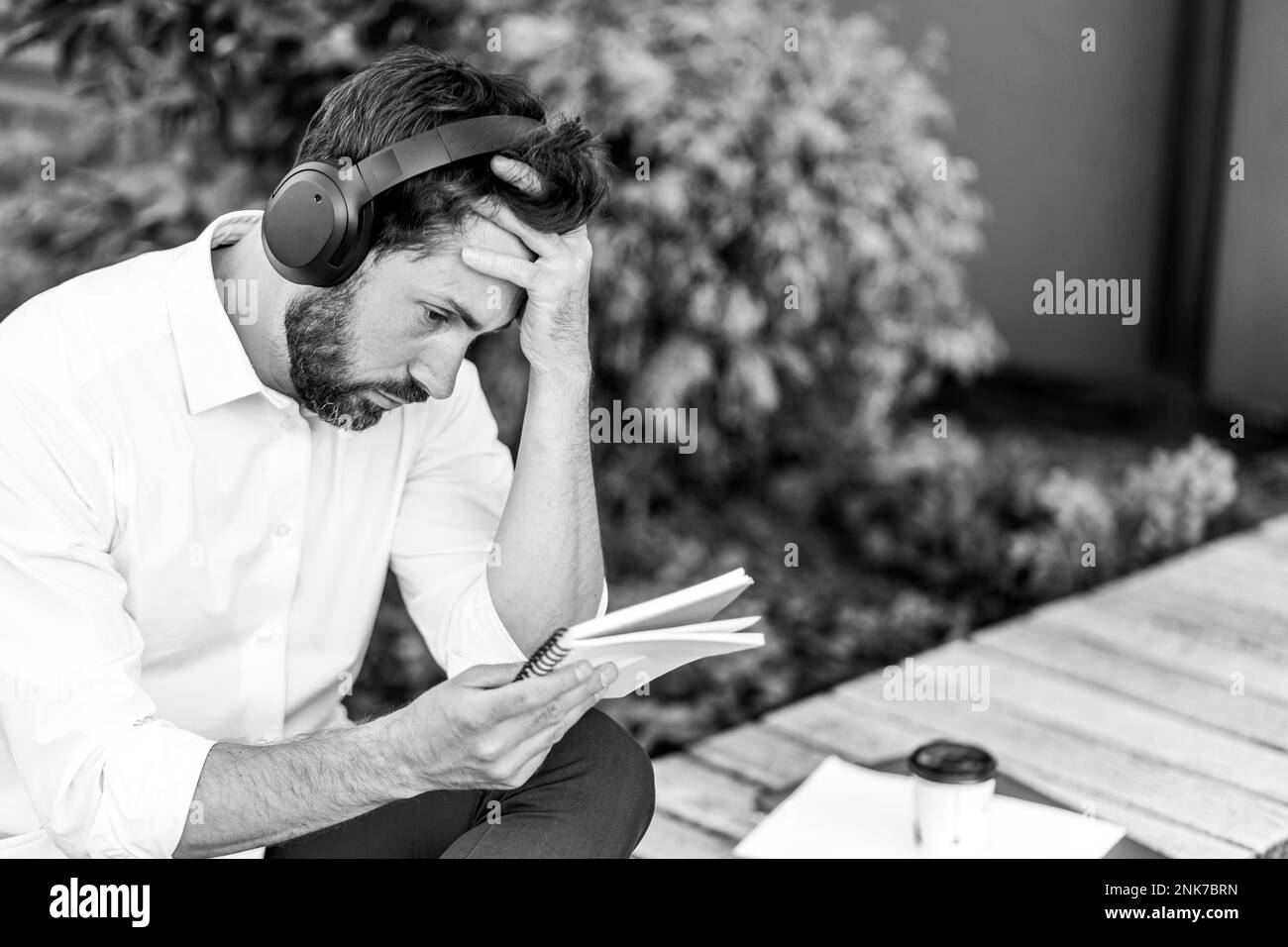 Thoughtful man in headphones checking notes, while sitting on bench ...