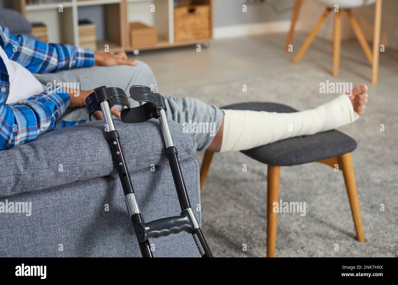 Crutches leaned on the couch, and a man with a cast on his broken leg ...