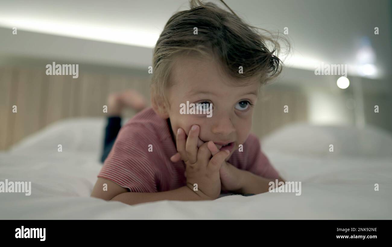 Hypnotized little boy watching TV screen at night laying in bed. Close ...