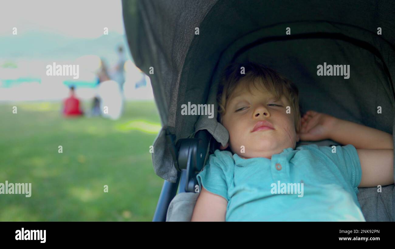 Sleeping child resting inside stroller at park during sunny day. One ...