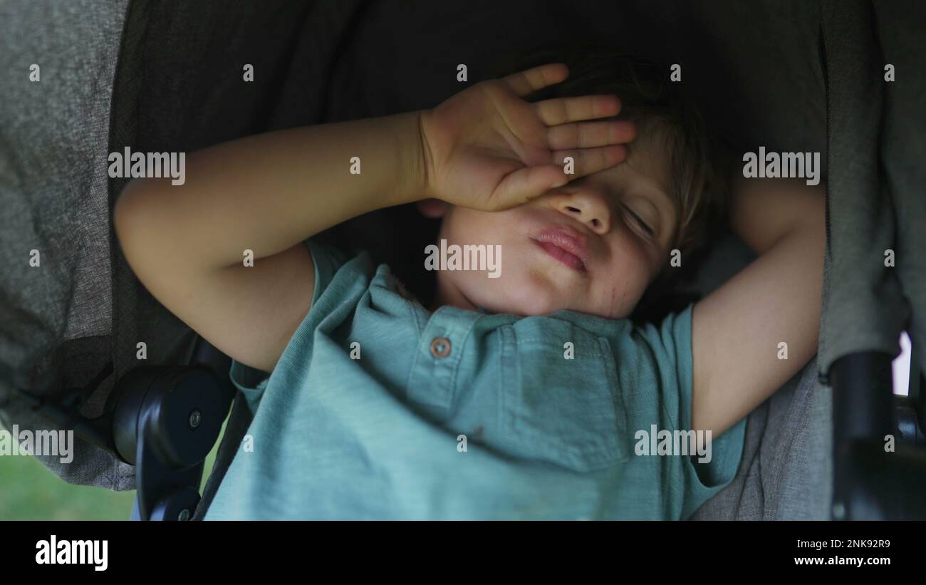 One tired small boy awake after nap sitting inside stroller. Exhausted child not wanting to get ...