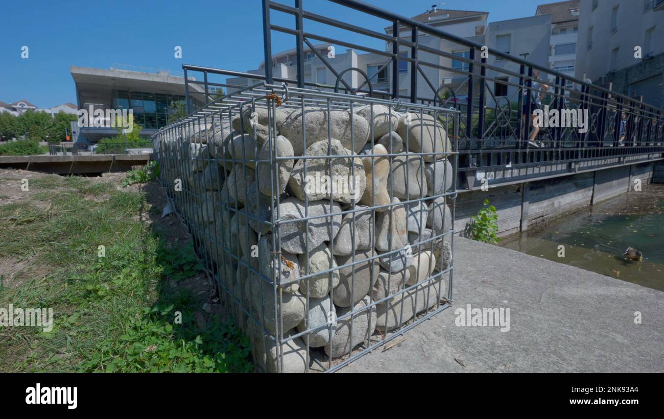 Many rocks stacked behind wire cage outside near bridge. Gray granite ...