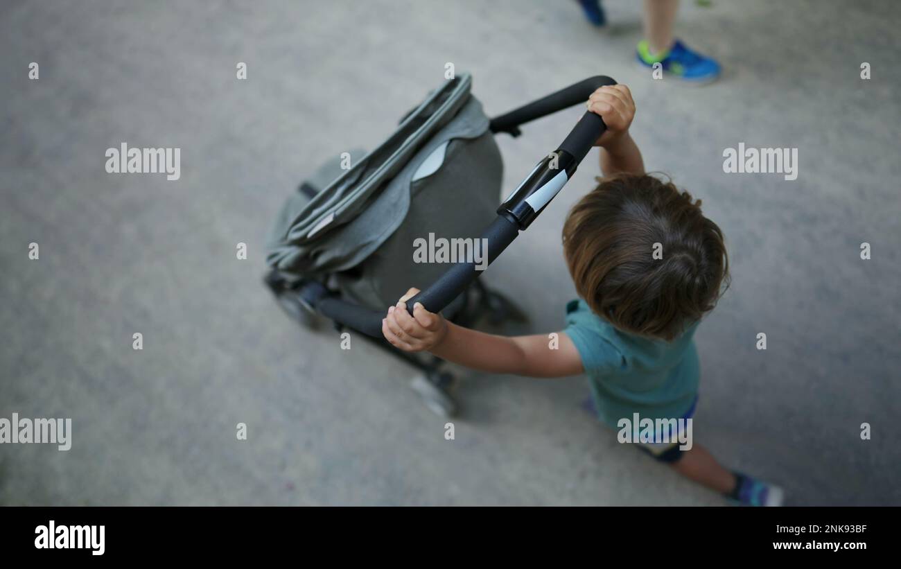 Top view of Cute child pushing stroller chair outside. Little boy ...