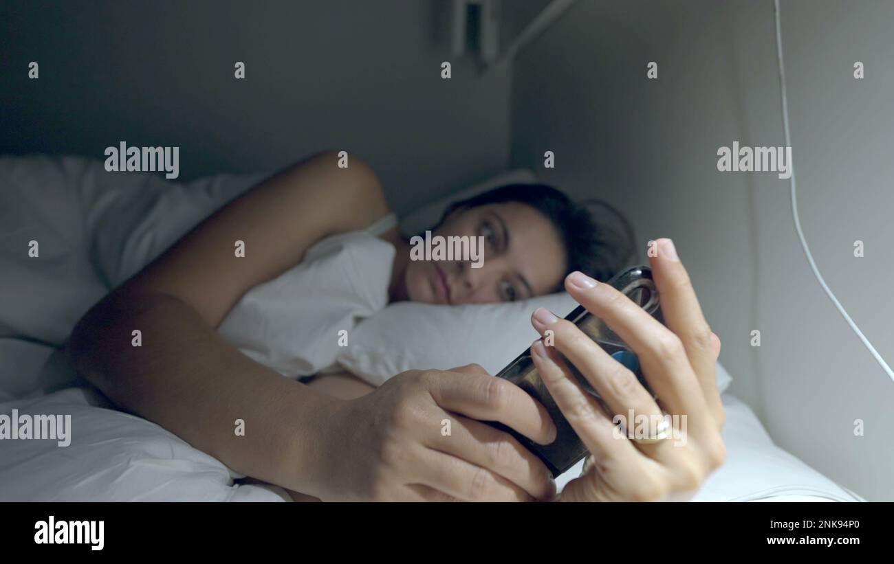 Woman staring at cellphone device at night in bed. Female person ...