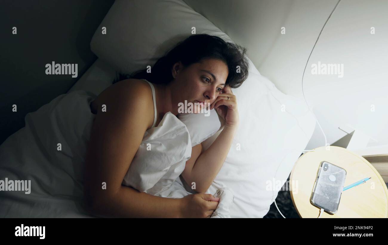 Woman laying in bed at night unable to sleep. Person turning light on ...